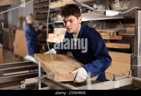 Young guy putting wooden board on cutting machine Stock Photo - Alamy