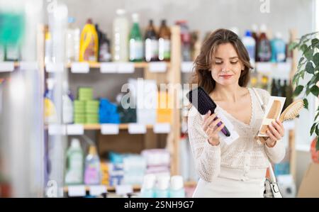 satisfied female customer deciding on make-up items on shelves in ...