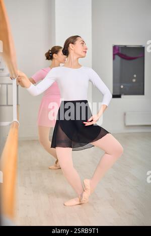 young ballerina in rehearsal wear stretching legs in choreography class ...