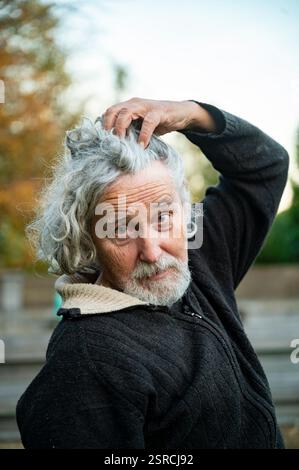 Mature man with grey beard making horn gesture and looking aside ...