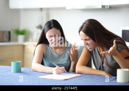 Angry interracial roommates reading a paper contract in the kitchen at ...