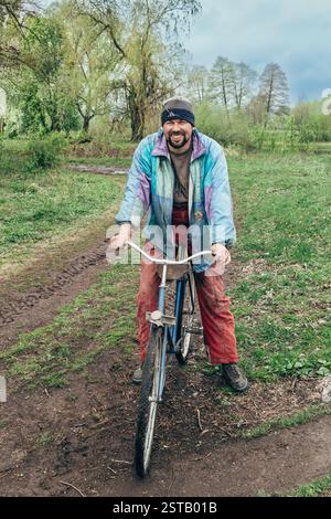 Ukraine, Romny, May 01, 2020: A farmer stands near a cow drinking water by a calm river ...