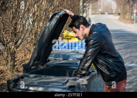 Attractive young man putting out rubbish standing with the lid up on a ...