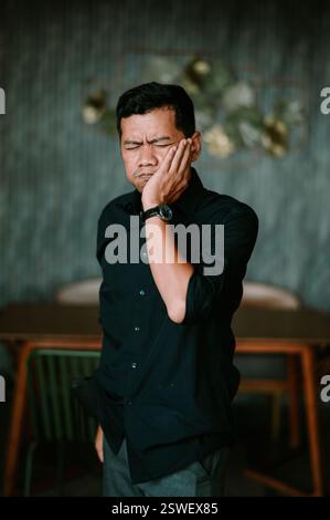 A man with a pained expression clutches his face, appearing to suffer ...