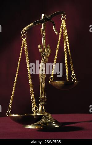 Empty unbalanced brass justice scales isolated on dark red background ...