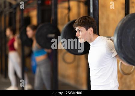 Slender guy trains muscles of arms and back using barbell and ...