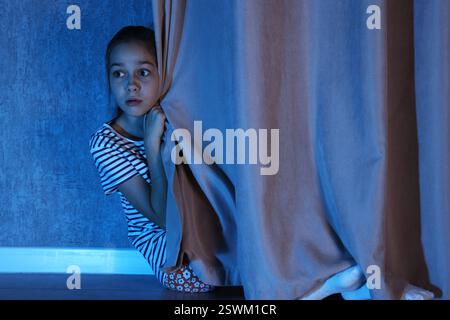 Scared girl hiding behind curtain at night Stock Photo - Alamy