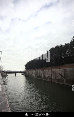 Stream of water bordered by concrete walls with a bridge afar and a ...