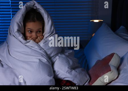 Afraid girl wrapped in duvet on bed at night. Space for text Stock ...
