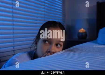 Scared girl hiding behind bed at night Stock Photo - Alamy