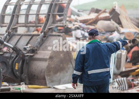 Landfill worker directing skid steer loader on the garbage heap. Waste ...