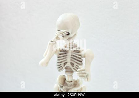 Human skeleton covers his face with his hand by white wall background ...