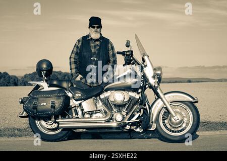 Kultiger Rocker mit seiner Harley-Davidson fährt auf einer Landstrasse ...