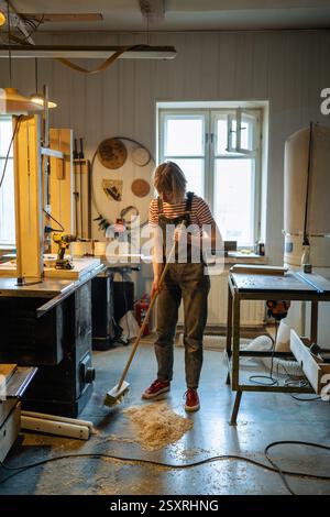 Carpenter woman cleaning up workshop after work. Handywoman sweep ...
