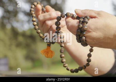 Close-up of a woman praying with a sunlit Buddhist wooden mala beads in ...