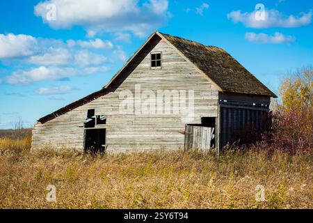 A large, old, abandoned building with a slanted roof. The sky is blue ...