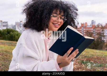 Woman with curly hair and glasses sitting on a park bench, reflecting ...