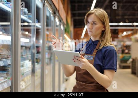 Grocery store worker using a tablet while arranging products on the ...