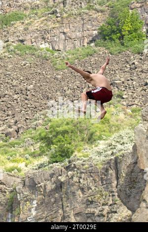 A young man is jumping off a cliff into the water below in Twin Falls ...