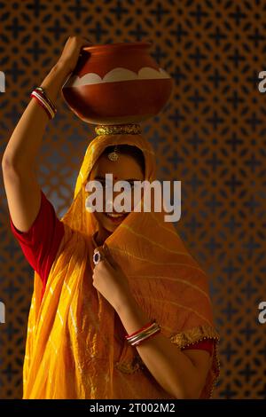 Portrait of a happy Rajasthani woman carrying clay pot on her head ...
