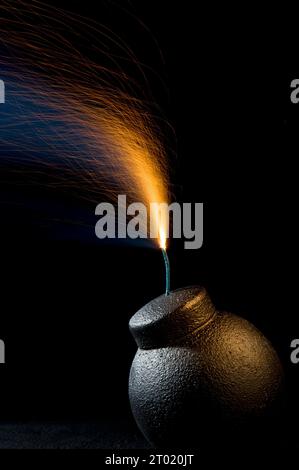 An old round cast iron bomb with lit fuse agaisnt a black background ...