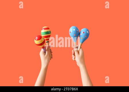 Female hands holding maracas on orange background Stock Photo - Alamy