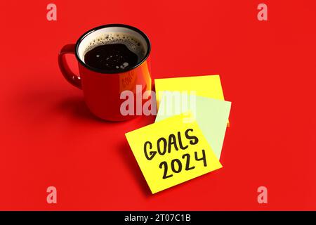 Sticky notes with goals for 2024 and cup of coffee on red background ...