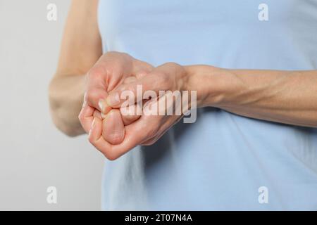 Woman cracking her knuckles on light grey background, closeup. Bad ...