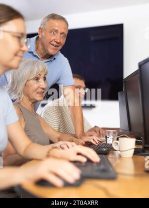 Friendly elderly computer course teacher helping woman learn computer ...