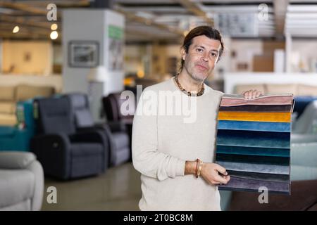 Male furniture salesman showing different fabric samples in furniture ...