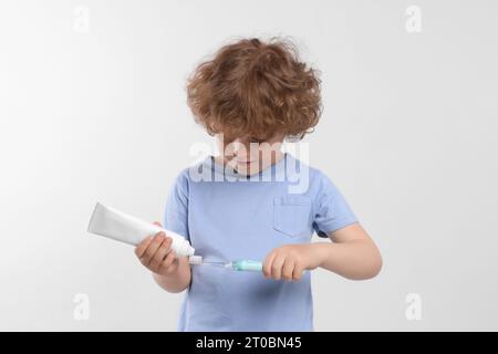 Cute little boy squeezing toothpaste from tube onto electric toothbrush ...