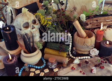 Old runes, mortar with herbs, candles and skull on witch altar table ...