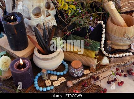 Old runes, mortar with herbs, candles and skull on witch altar table ...