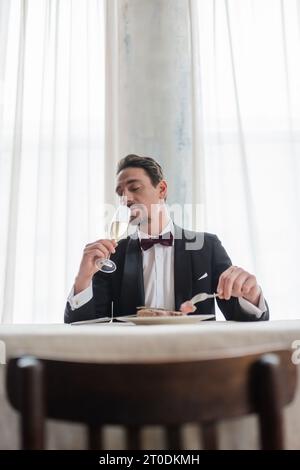 wealthy gentleman in tuxedo eating delicious beef steak near glass of ...
