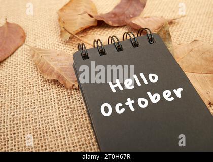 "Hello October" writing on spiral black notebook on burlap with ...