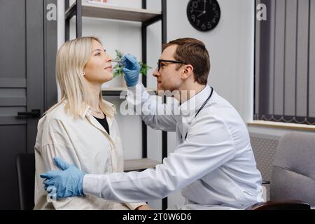 A young attractive otolaryngologist examining nose of a young patient ...