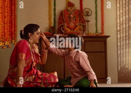 Son applying tilaka to forehead of his mother on the occasion of Ganesh ...