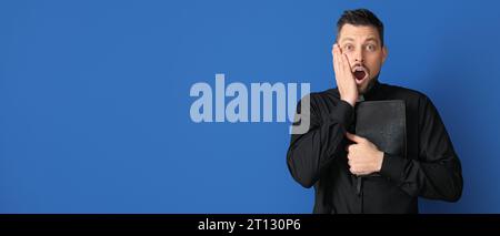 Surprised priest holding Bible on orange background with space for text ...