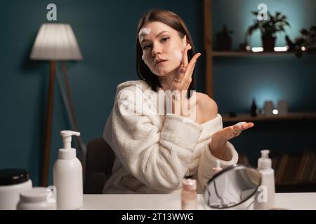 beauty blogger applying face foam on hand near gadgets and ring lamp ...