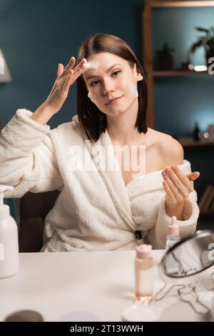 beauty blogger applying face foam on hand near gadgets and ring lamp ...