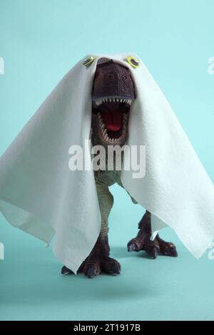 a plastic t-rex dinosaur figurine disguised as a ghost with a sheet and ...