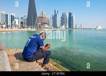 Man sits on steps of Corniche with skyscrapers in background, West Bay ...