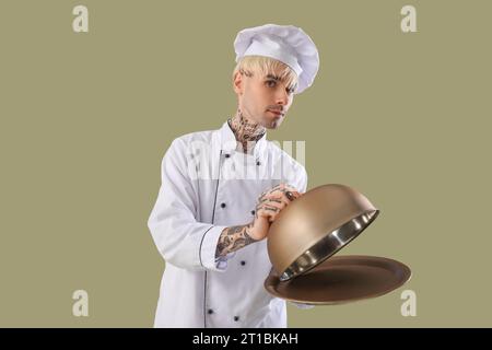 Tattooed male chef with cloche on green background Stock Photo - Alamy