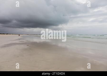 A vast beach is blanketed by grey, stormy clouds, and their reflection ...