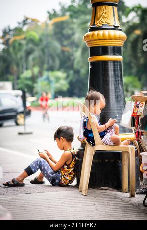 Two young Filipino children enjoy something on their mobile phones sat ...
