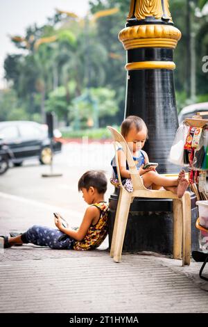 Two young Filipino children enjoy something on their mobile phones sat ...