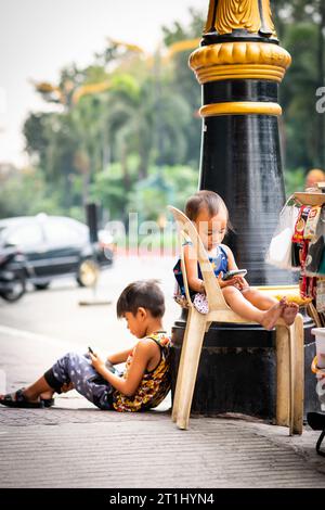 Two young Filipino children enjoy something on their mobile phones sat ...