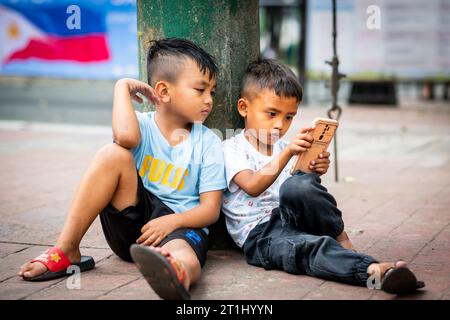 Two young Filipino boys enjoy something on their mobile phone sat ...