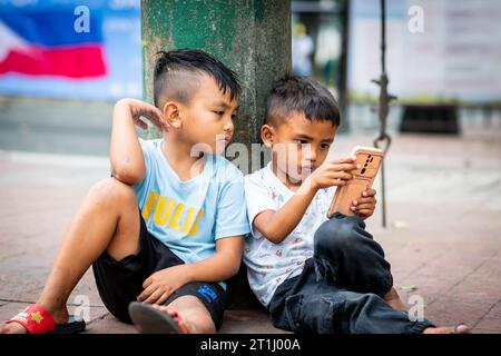 Two young Filipino children enjoy something on their mobile phones sat ...
