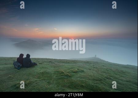 A couple watch a cloud inversion at sunrise on Mam Tor in Derbyshire ...